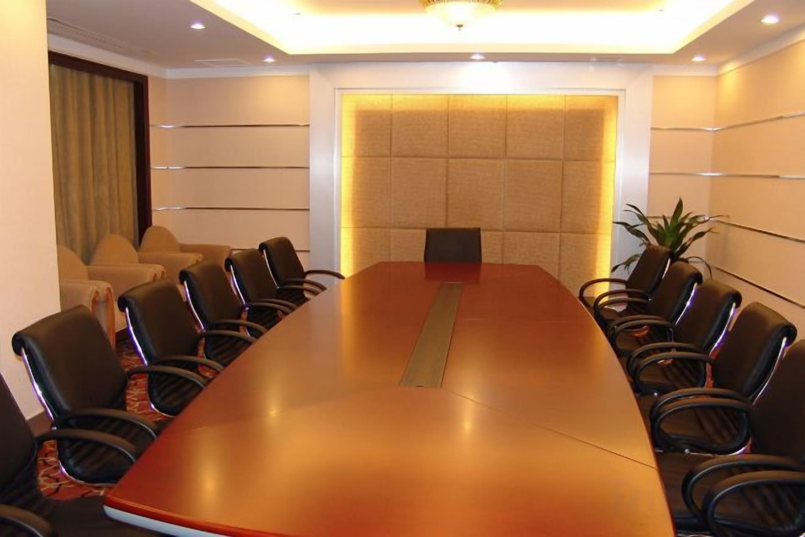 Sala de conferências com uma mesa comprida, cadeiras, uma planta e uma janela grande.