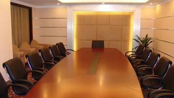 Sala de conferências com uma mesa comprida, cadeiras, uma planta e uma janela grande.