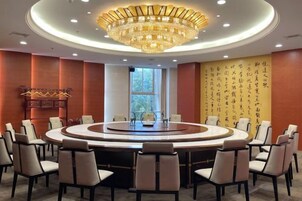 Uma sala de conferências com uma mesa redonda, cadeiras, um candelabro e uma janela grande.