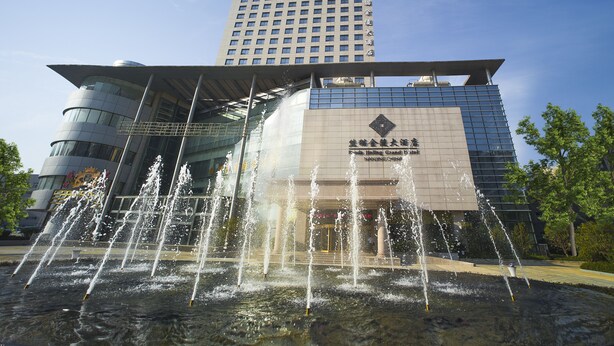 Um hotel com design moderno, apresentando uma fonte na frente e um edifício grande ao fundo.