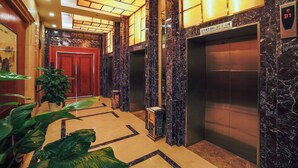 Um saguão de hotel com paredes de mármore, uma porta vermelha e um elevador.