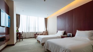 Quarto de hotel com duas camas, uma escrivaninha, uma cadeira, uma televisão e uma janela grande com cortinas.