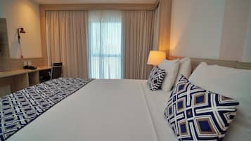 Quarto de hotel com uma cama grande, uma escrivaninha com telefone e uma luminária.