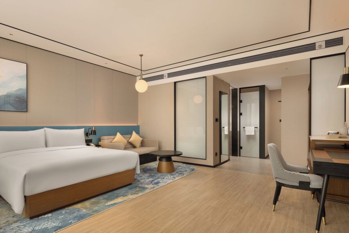 Quarto de hotel moderno com uma cama grande, uma escrivaninha, uma cadeira e um sofá.
