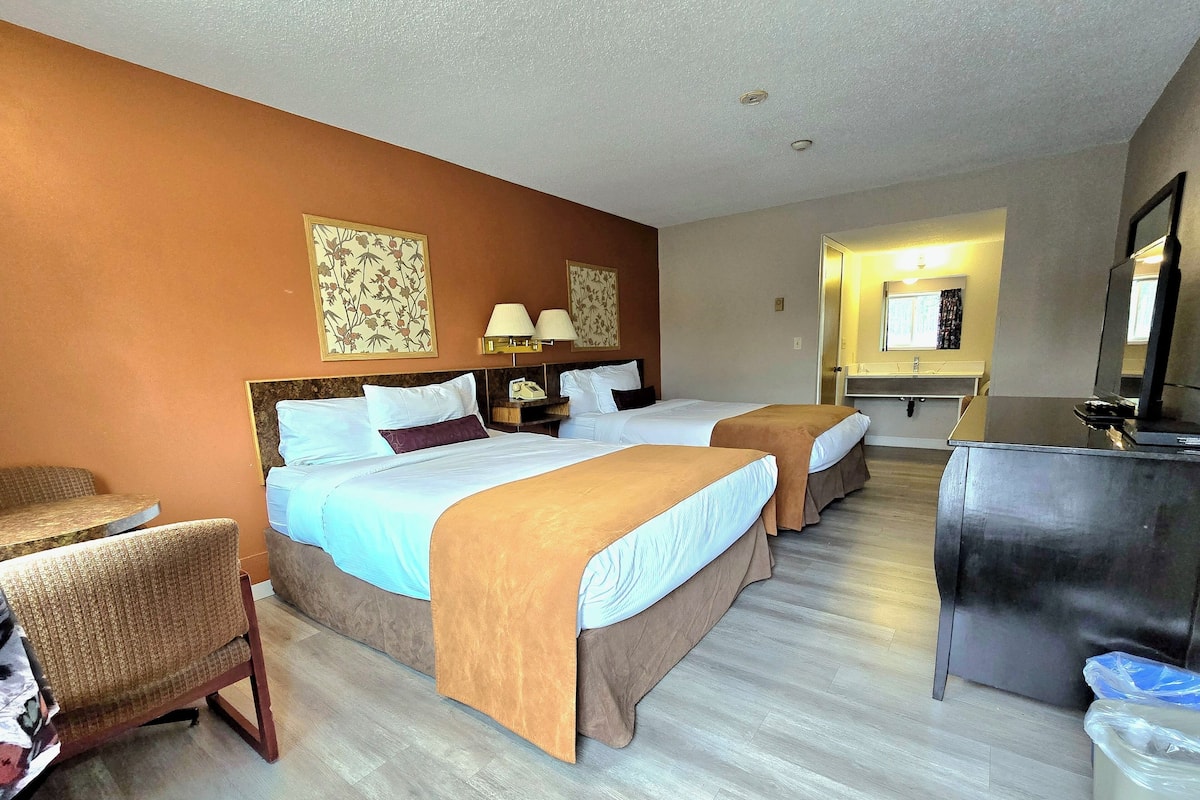 Quarto de hotel com duas camas, uma escrivaninha, uma cadeira e um espelho.