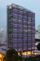 Um edifício alto com design arquitetônico moderno, apresentando uma grade de janelas e iluminação roxa na fachada.