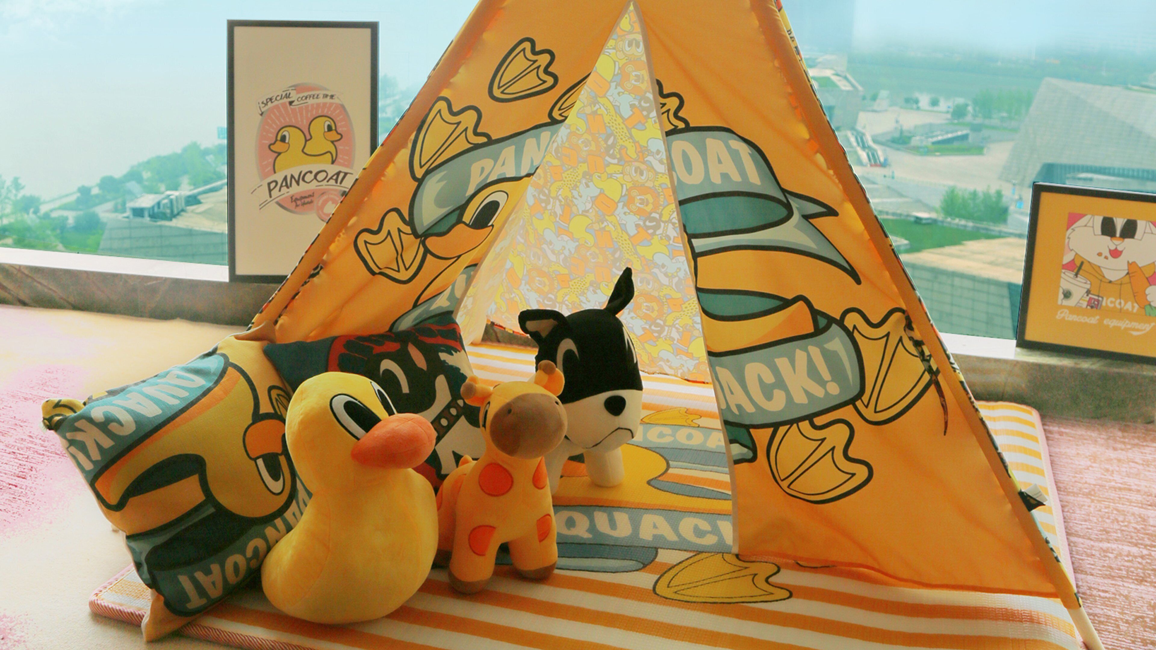 Uma tenda com personagens de desenho animado e a palavra "Pancoa" sobre ela, colocada sobre uma cama com vista para a janela.