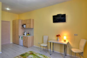 Um espaço compacto com cozinha americana, área de jantar com duas cadeiras, pequena mesa com abajur e TV fixada na parede.