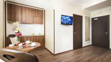 Quarto de hotel moderno com uma mesa de jantar de madeira, uma TV fixada na parede e uma porta de madeira escura.