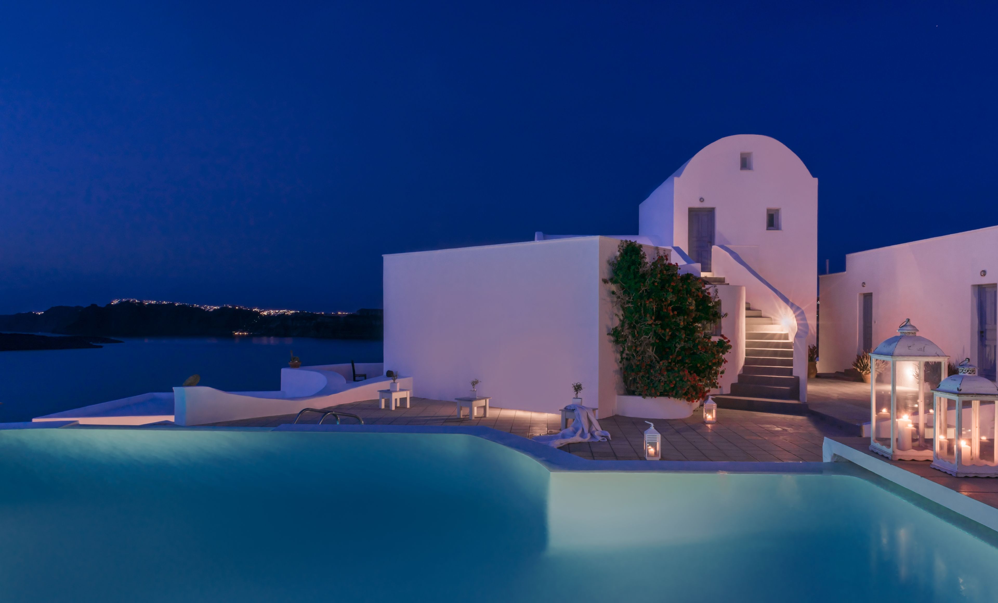 Um edifício moderno branco com piscina, escadaria e vista para o mar ao anoitecer.