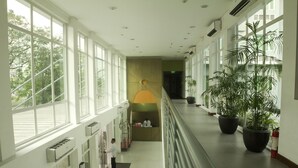 Corredor de hotel com grandes janelas, plantas em vasos e aparelhos de ar condicionado.