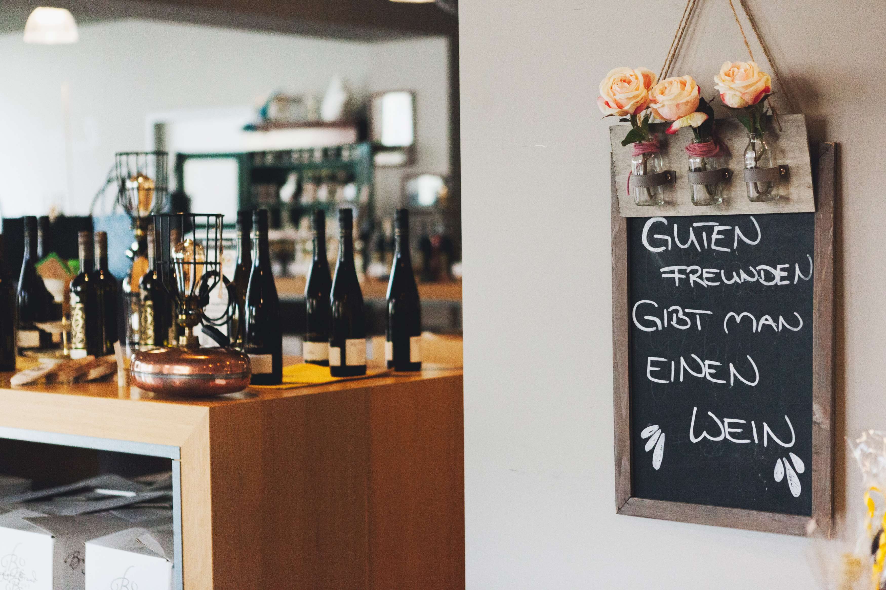 Uma área de bar com garrafas e copos, e um quadro negro com rosas e texto.