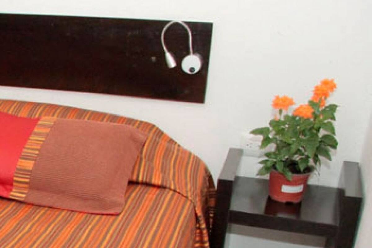 Uma cama com roupa de cama listrada, cabeceira escura e mesa de cabeceira com uma planta em vaso.