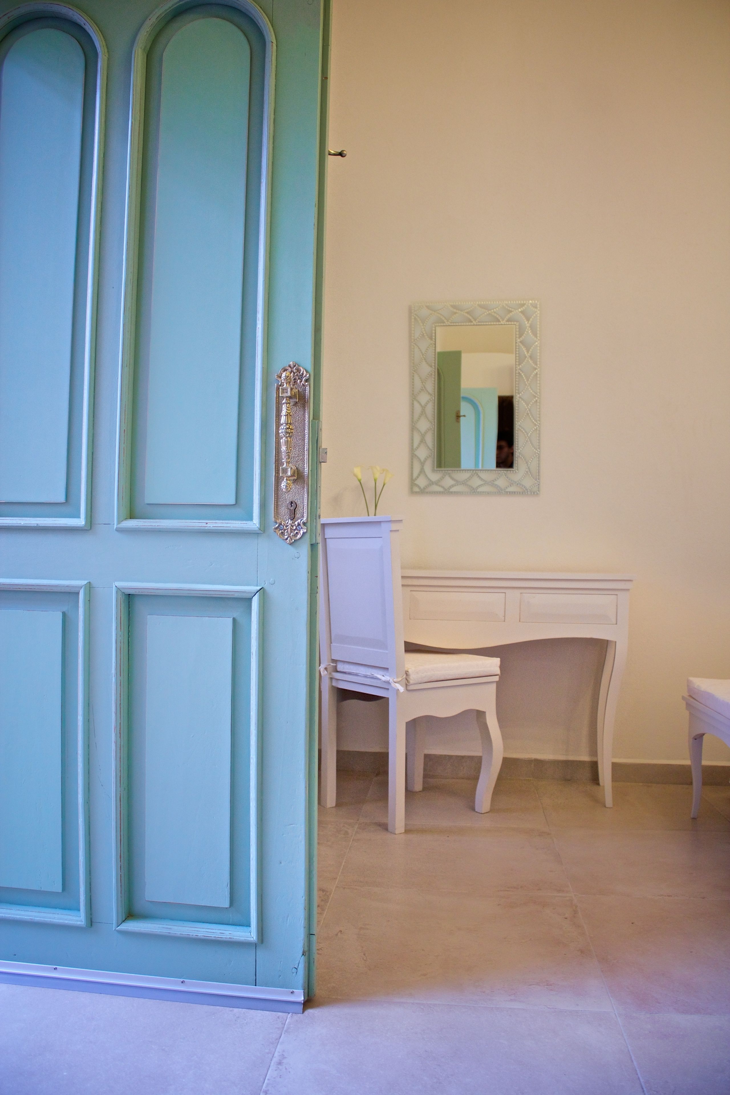 Quarto com porta azul-turquesa, escrivaninha branca, cadeira e um banquinho.