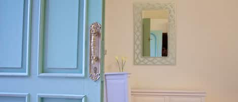 Quarto com porta azul-turquesa, escrivaninha branca, cadeira e um banquinho.