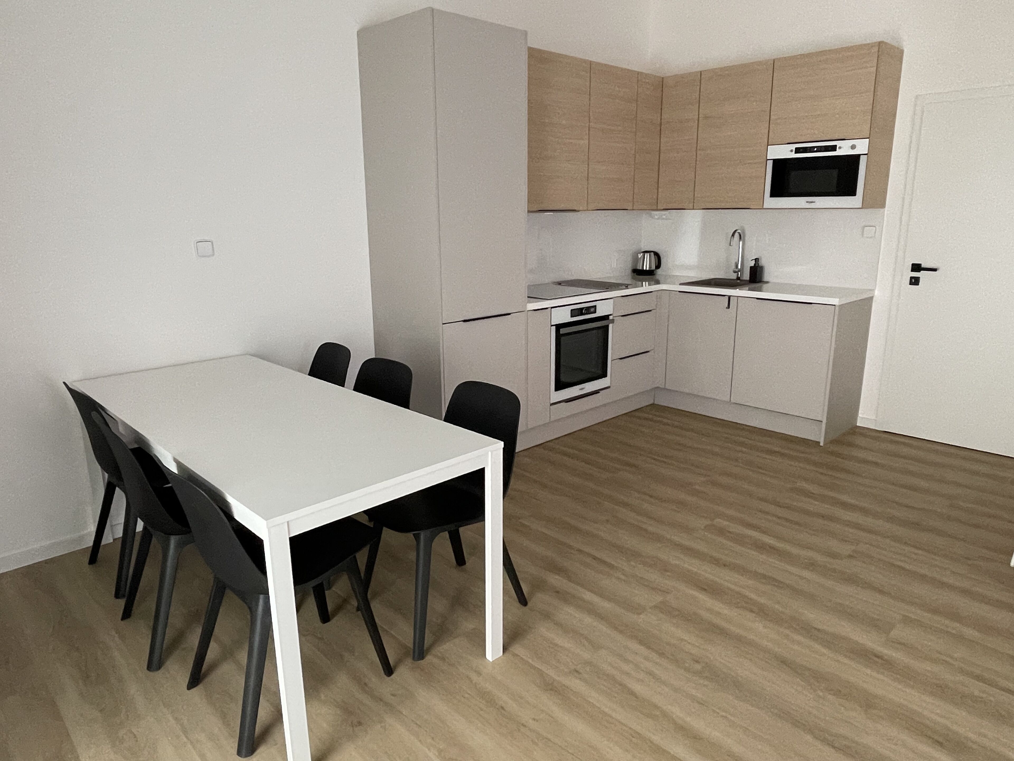 Uma cozinha compacta com uma mesa e cadeiras brancas, micro-ondas, forno e pia.