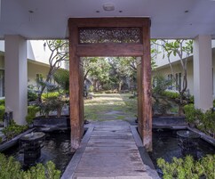 Um arco de madeira que dá acesso a um jardim com um elemento aquático e plantas em vasos.