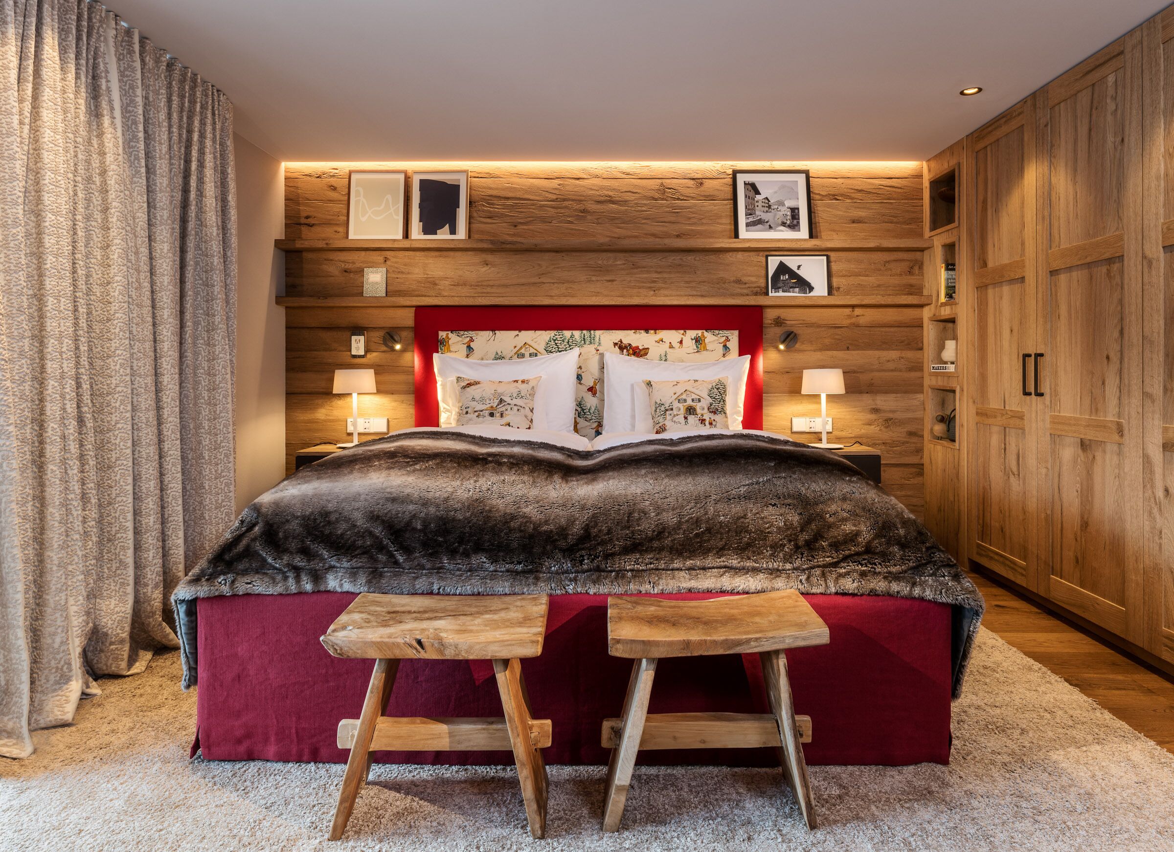 Quarto com cabeceira de madeira, parede em destaque na cor vermelha, cama grande com manta de pele, duas mesas de cabeceira com abajures e armários de madeira.