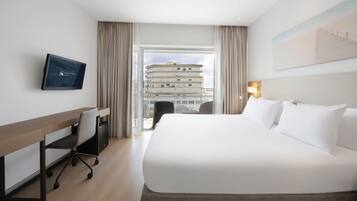 Quarto de hotel com cama, escrivaninha, cadeira, televisão e vista para edifícios.