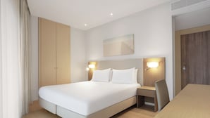 Quarto de hotel com uma cama grande, mesas de cabeceira, uma escrivaninha e uma cadeira.