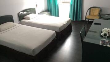 Quarto de hotel com duas camas de solteiro, uma escrivaninha com cadeira e uma janela com cortinas.