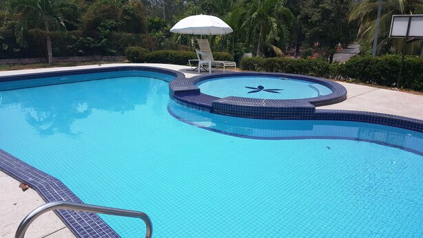 Uma piscina com borda em azulejo, um guarda-sol e uma espreguiçadeira.