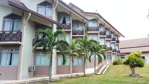 Um hotel com vários andares, varandas, aparelhos de ar condicionado e um jardim bem cuidado.
