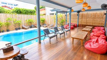 Uma área à beira da piscina com piso de madeira, espreguiçadeiras e pufes vermelhos.