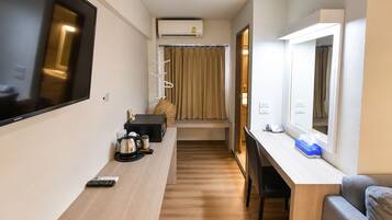 Quarto de hotel compacto com TV de tela plana, escrivaninha com cadeira, pequena cozinha e área de estar com sofá.