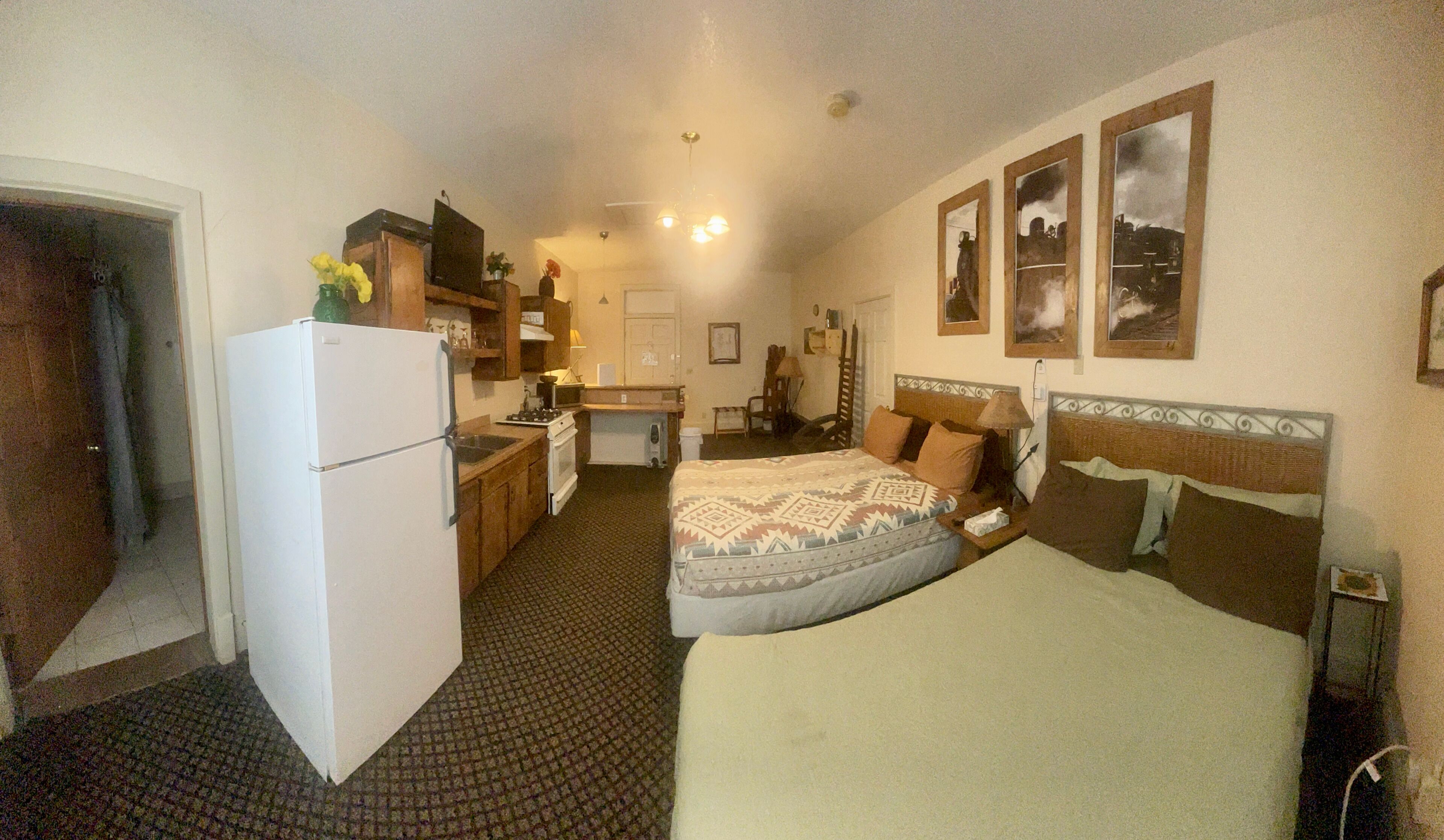 Quarto de hotel pequeno com cozinha compacta, cama com roupa de cama estampada e uma pequena área de trabalho.