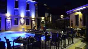 Vista noturna de um hotel com piscina, área de estar externa e paredes iluminadas.