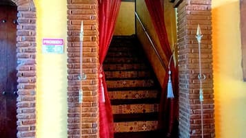 Uma escadaria com um arco de tijolos, uma cortina vermelha e um aviso de 'PROIBIDO'.