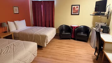 Quarto de hotel com uma cama, duas cadeiras, uma escrivaninha com computador, televisão e micro-ondas.