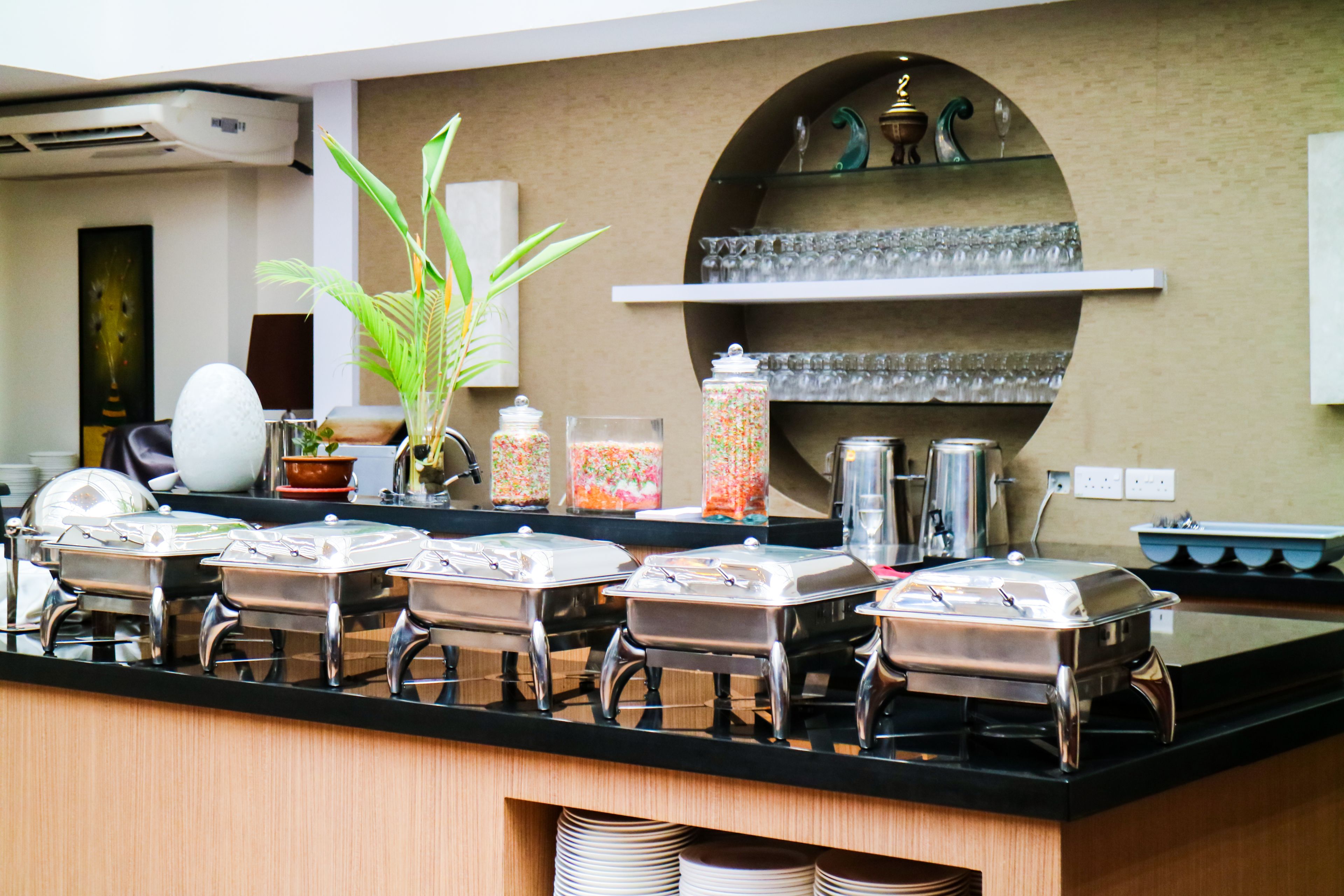Uma mesa de buffet com diversas estações de serviço, uma máquina de café e uma planta decorativa.