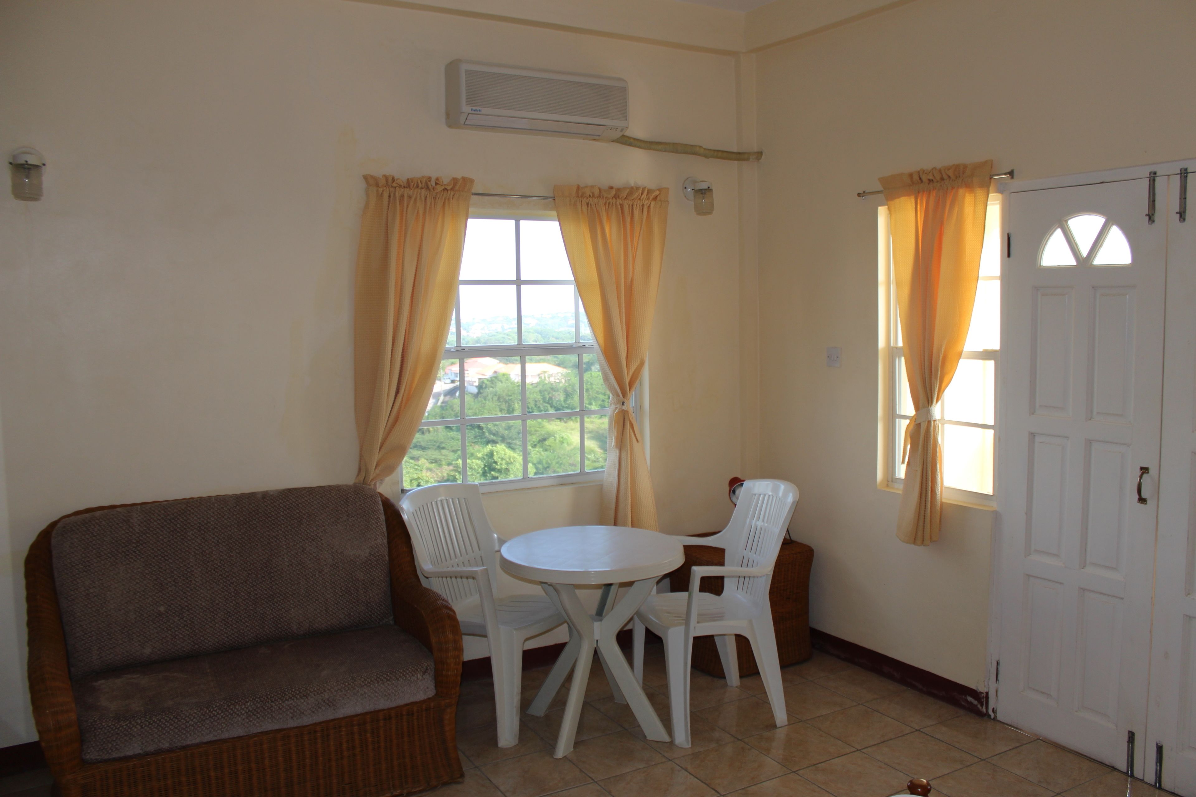 Um quarto com um sofá marrom, duas cadeiras brancas, uma mesa redonda pequena e uma janela com cortinas.