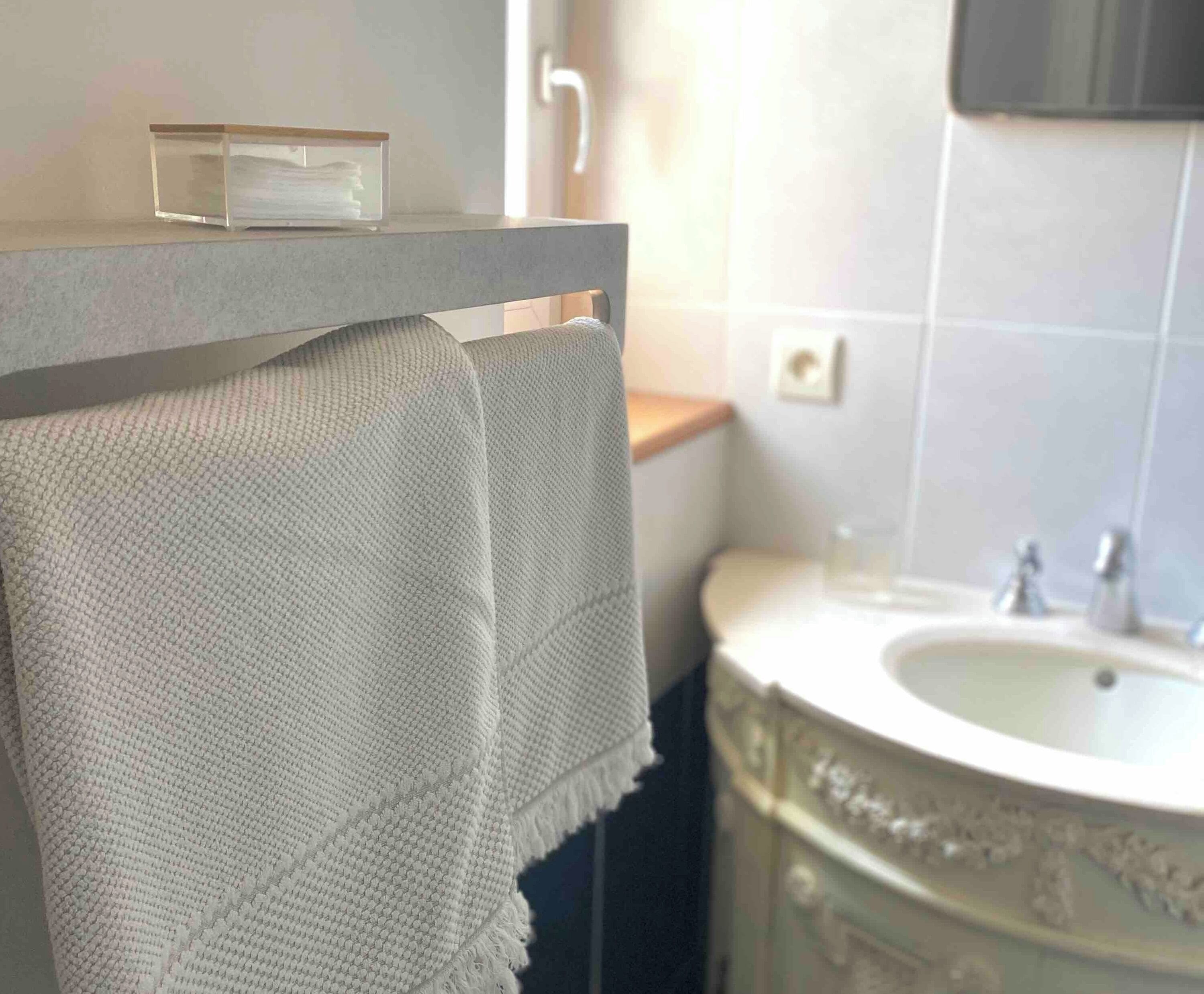 Um banheiro com uma toalha branca pendurada em um porta-toalhas, uma pia e um espelho.