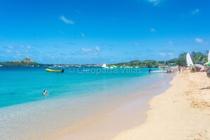 Uma praia com águas azul-turquesa cristalinas, areal arenoso e barcos.