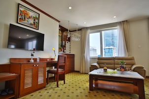 Quarto de hotel com televisão de tela plana, escrivaninha de madeira, sofá e mesa de jantar com frutas.