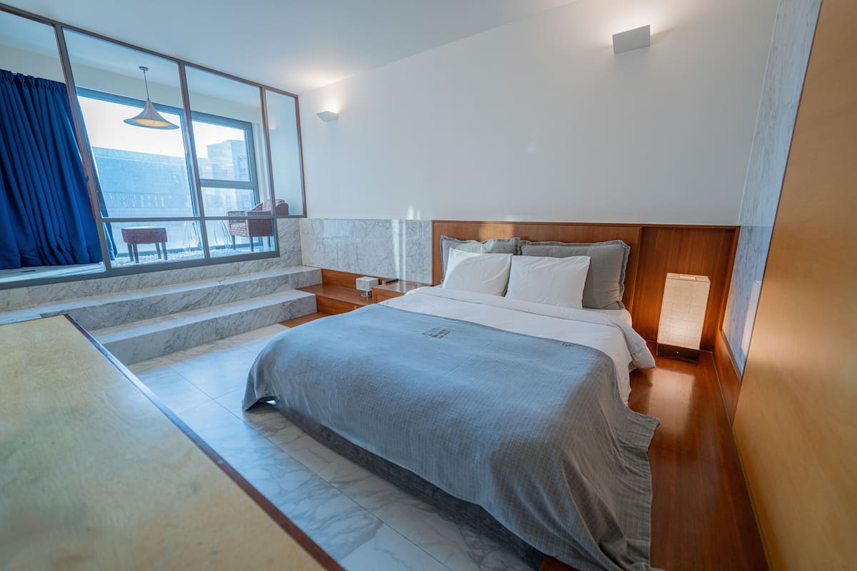 Quarto de hotel moderno com uma cama grande, área de estar com vista e escada que leva a um terraço ao ar livre.