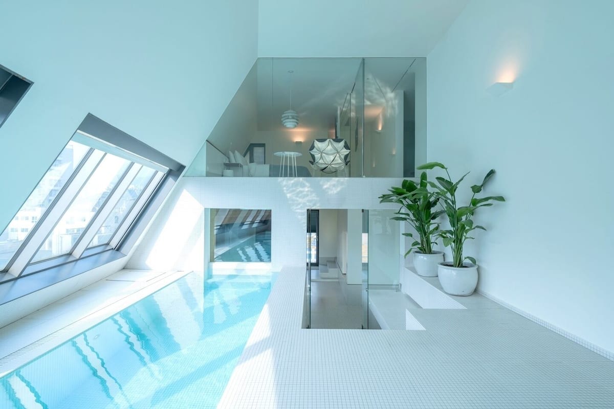Uma piscina interior moderna com paredes de vidro, um mezanino e plantas em vasos.