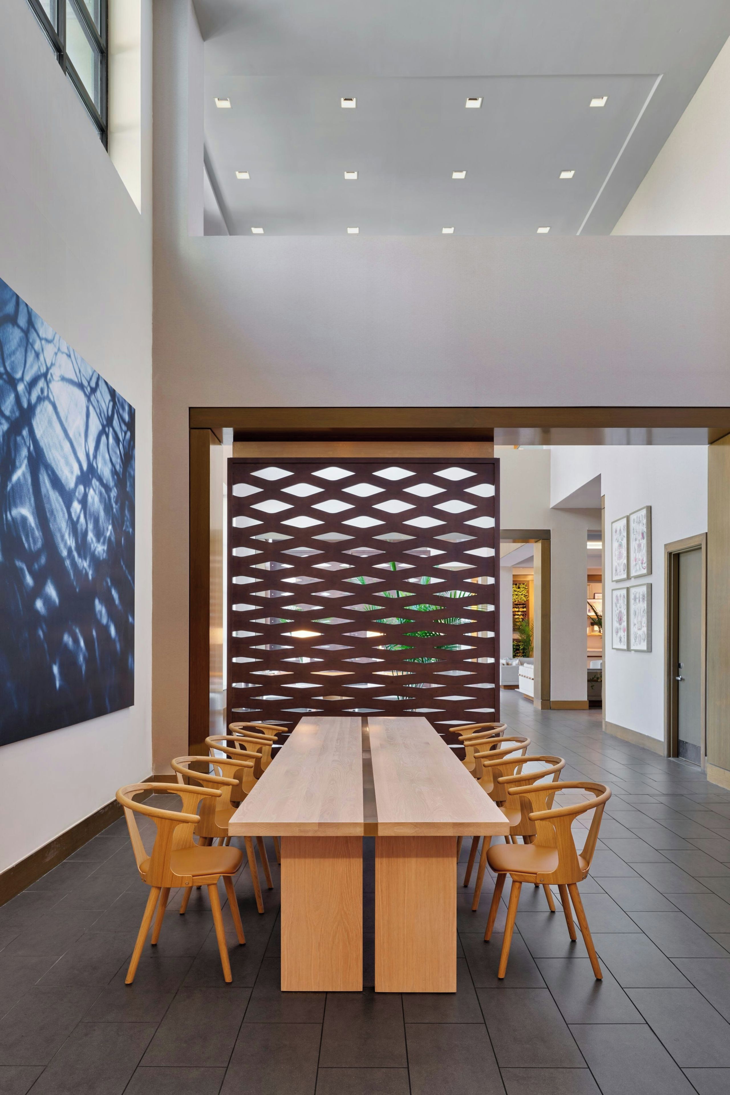 Uma sala de conferências moderna com uma mesa comprida, cadeiras de madeira e um divisório decorativo com recortes geométricos.