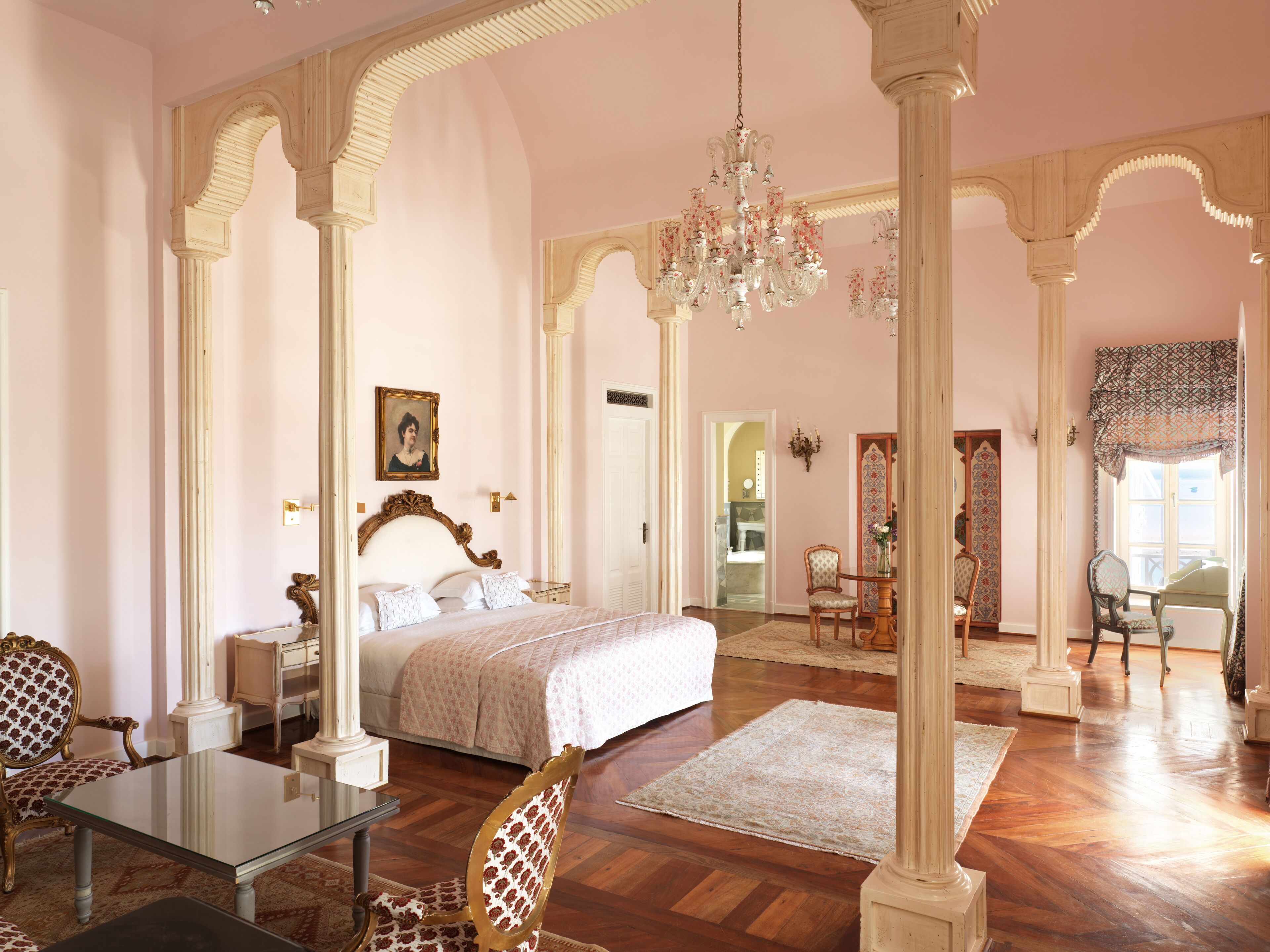 Um quarto espaçoso com uma cama grande, uma mesa de vidro e um candelabro.