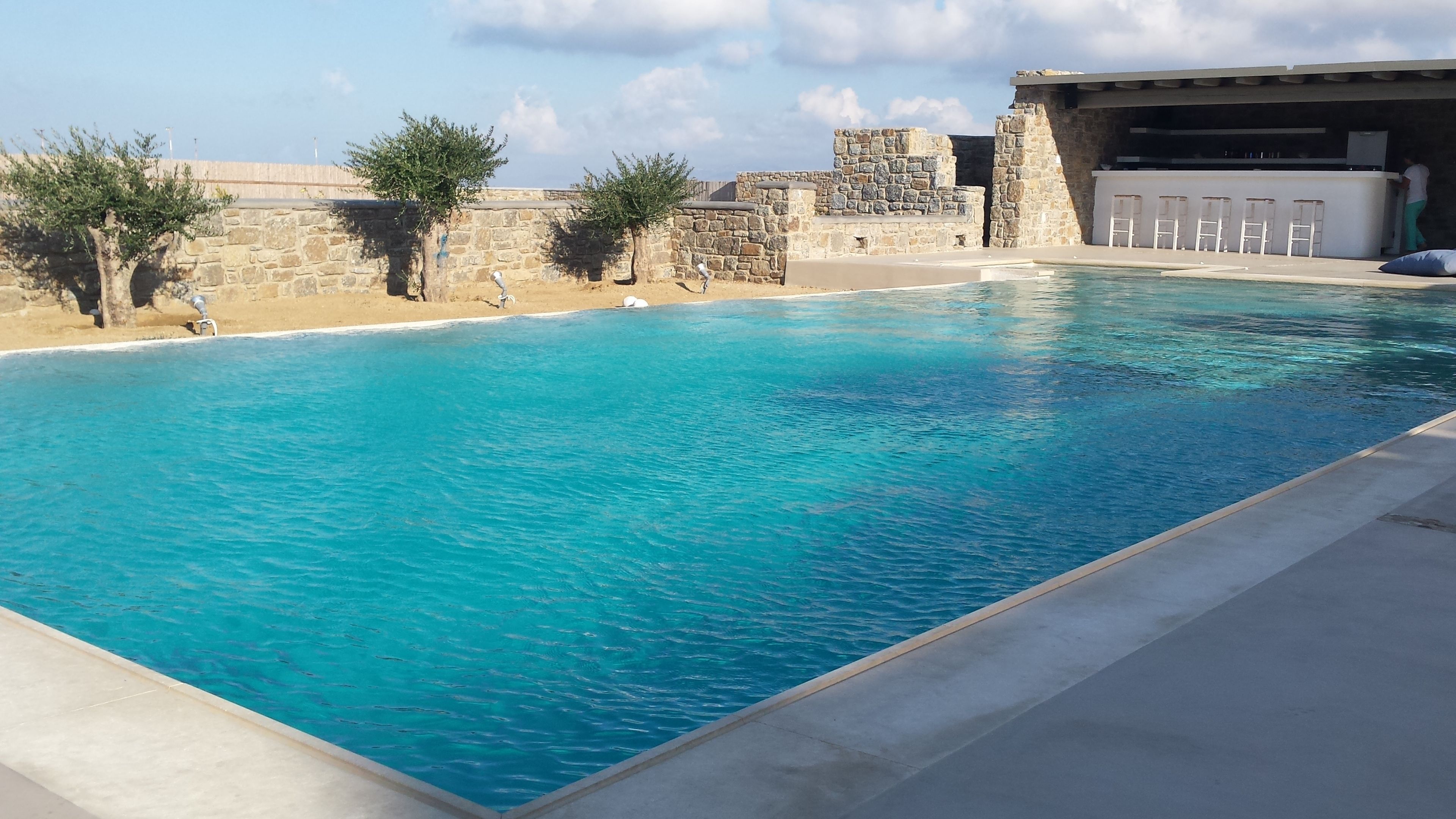 Piscina com água azul cristalina, rodeada por paredes de pedra e algumas árvores.