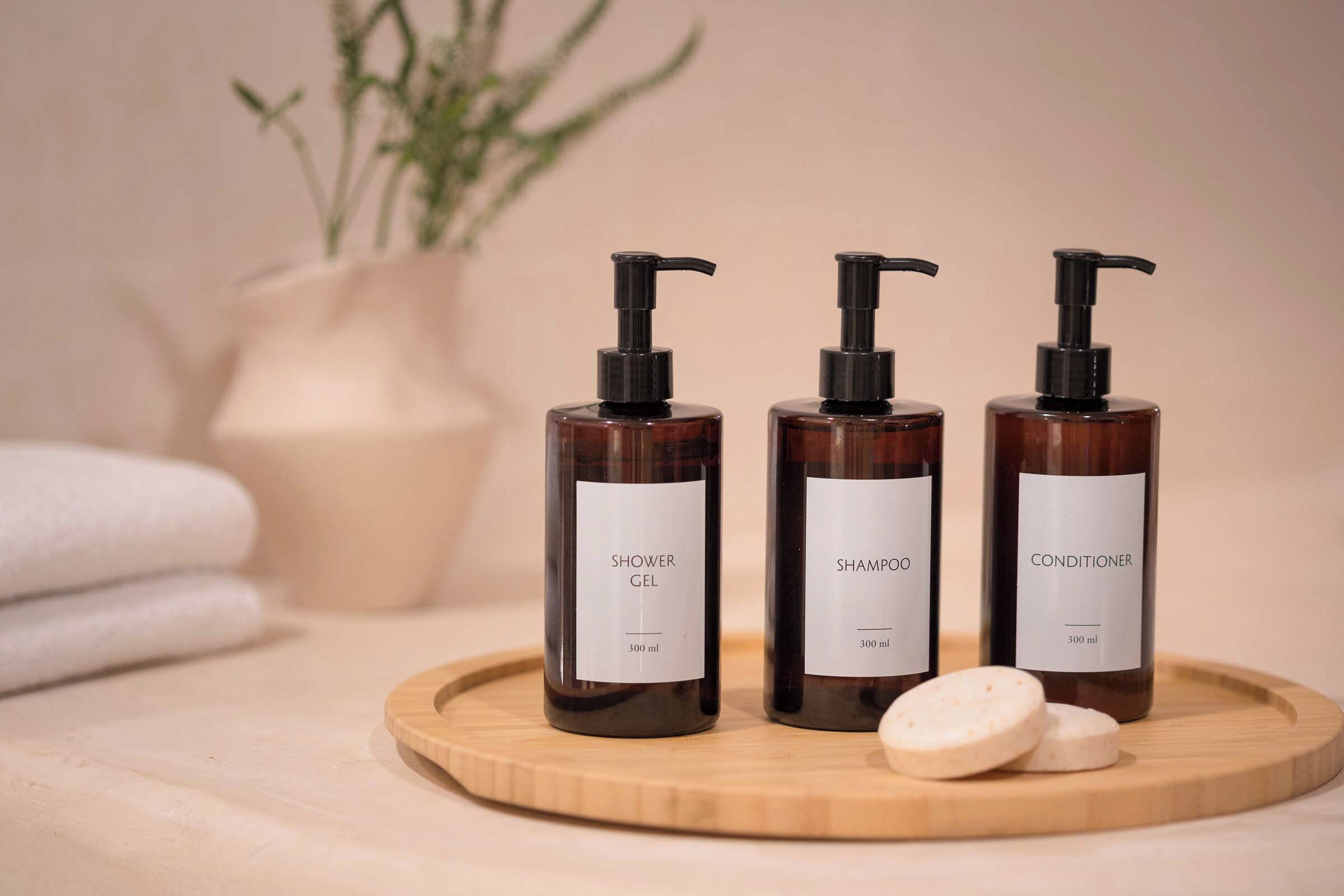 Três frascos de gel de banho, shampoo e condicionador sobre um tabuleiro de madeira.