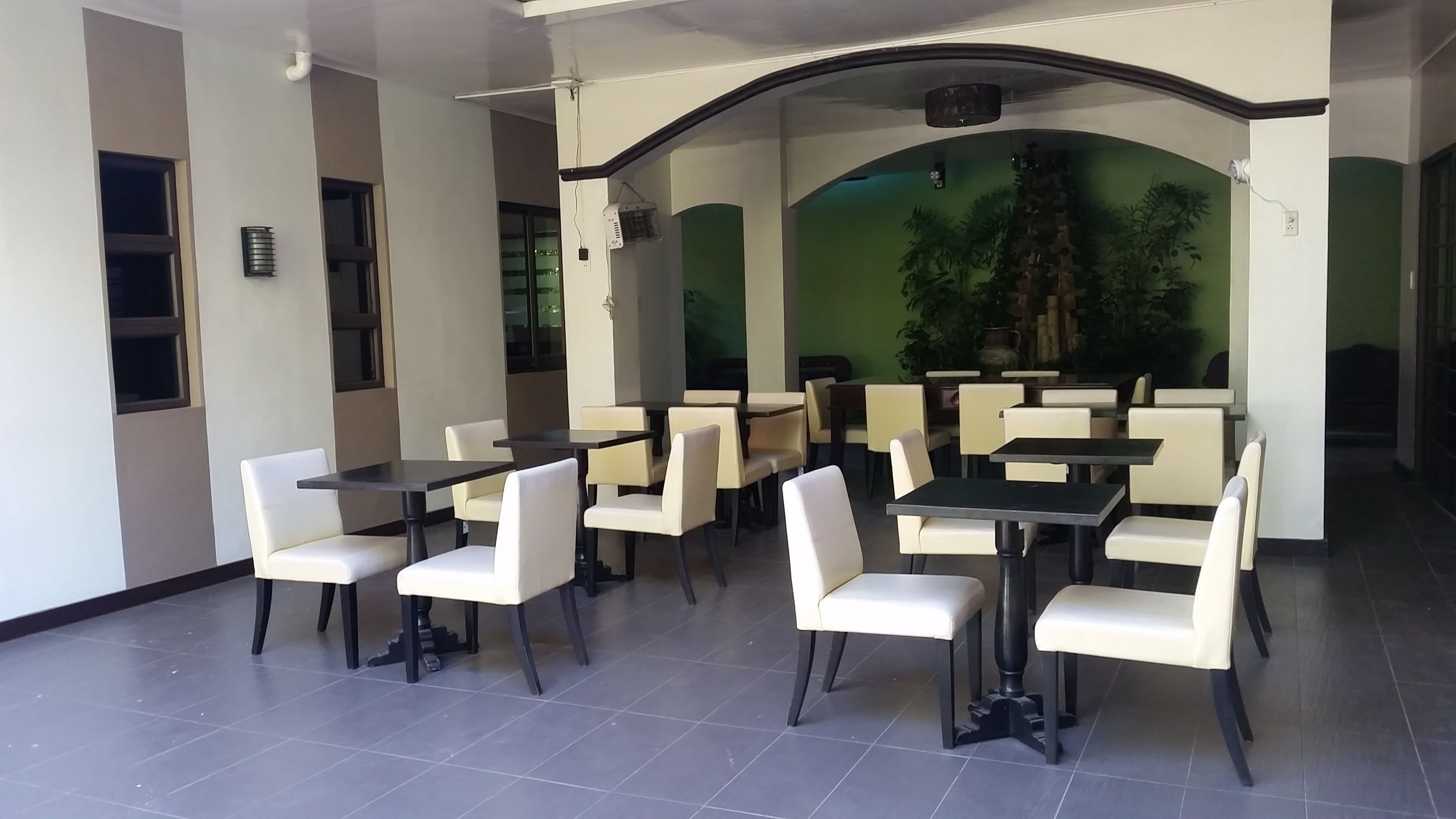 Uma área de refeições com mesas e cadeiras, uma parede verde com plantas e piso de azulejos.