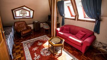 Quarto com sofá vermelho, poltrona de couro, mesa de centro de madeira, tapete estampado e janela com cortinas.