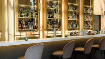 Uma área de bar com várias prateleiras de garrafas de bebidas, um balcão e banquetas.