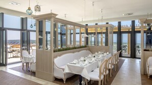 Um restaurante com uma mesa comprida posta para refeições, grandes janelas com vista e um espaço de estar acolhedor com um banco.