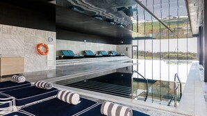 Uma área de spa moderna com uma piscina infinita de vidro, espreguiçadeiras e vista para a paisagem.
