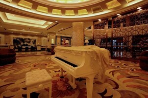Um hall imponente com um piano de cauda, um banquinho estofado e um bar com degustação de vinhos.